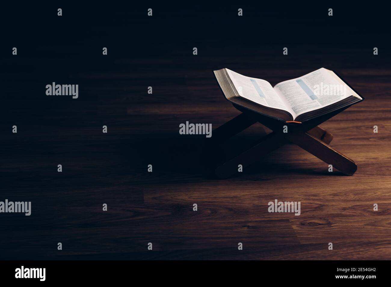 open bible on a book stand on a black background with a wooden floor ...