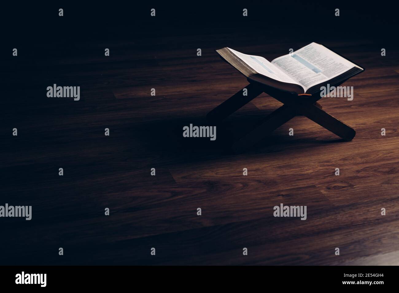 open bible on a book stand on a black background with a wooden floor ...