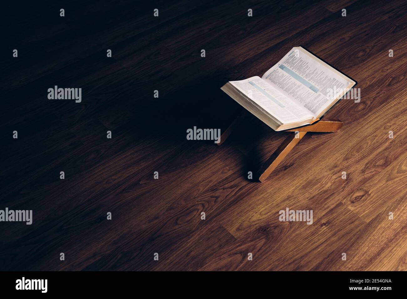 open bible on a book stand on a black background with a wooden floor ...