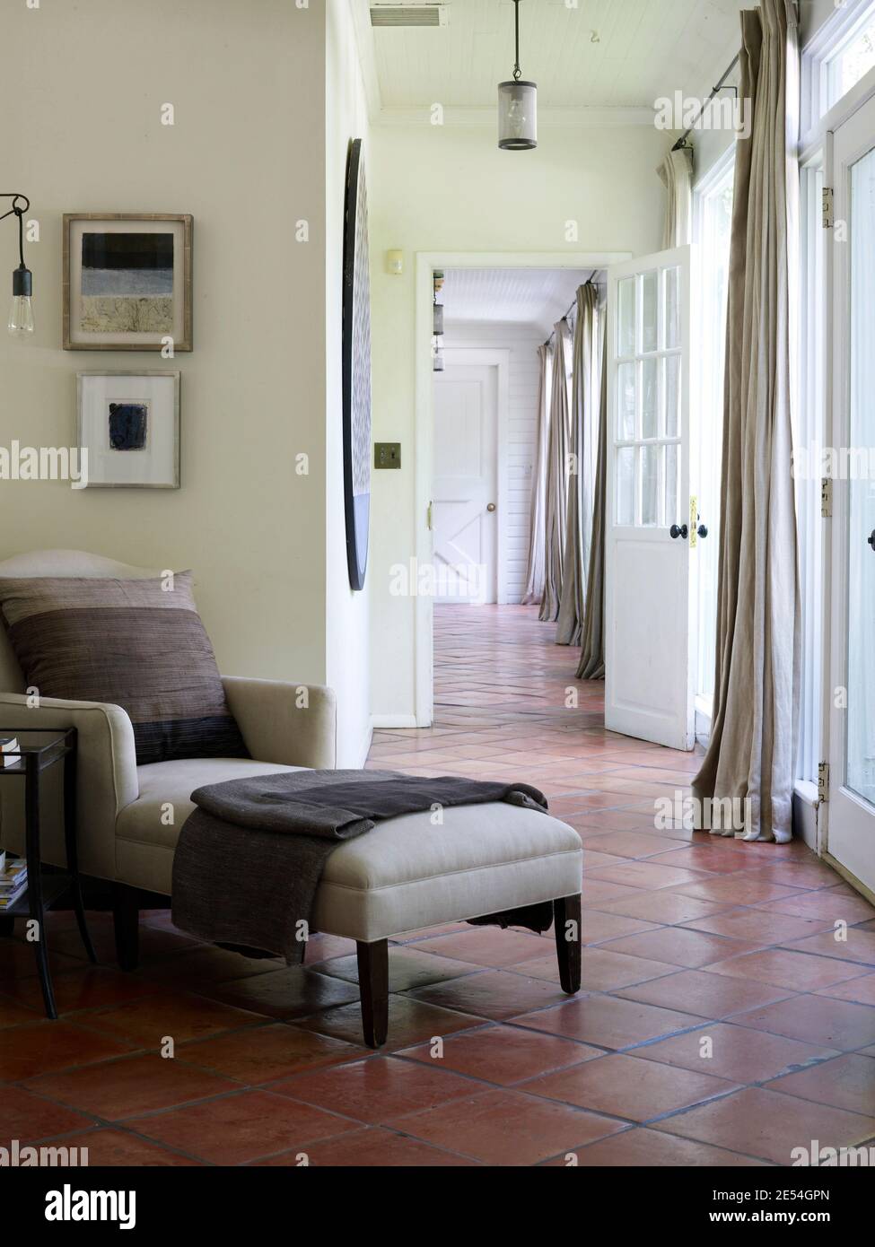 Armchair and footstool in terracotta tiled hallway in home of Francine ...