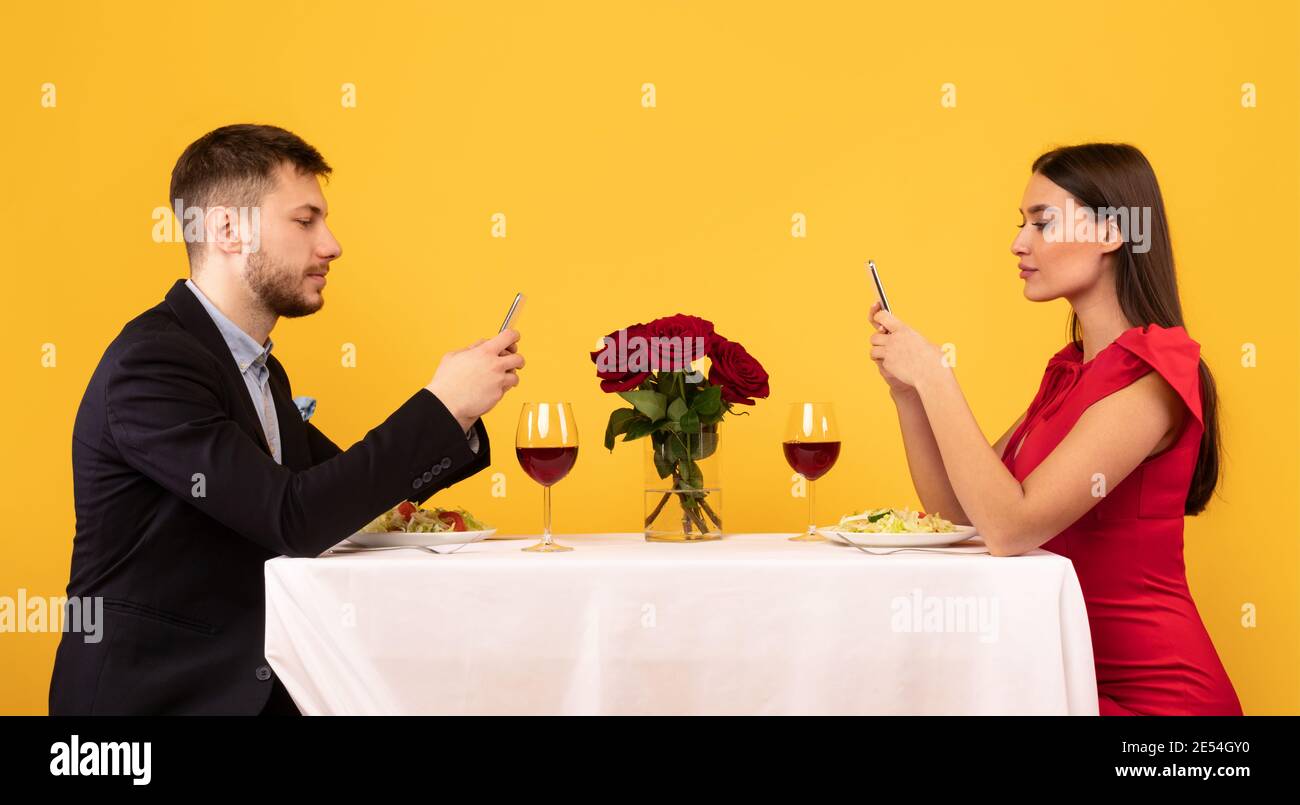 Couple Using Mobile Phones On Date In Restaurant, Studio Shot Stock ...