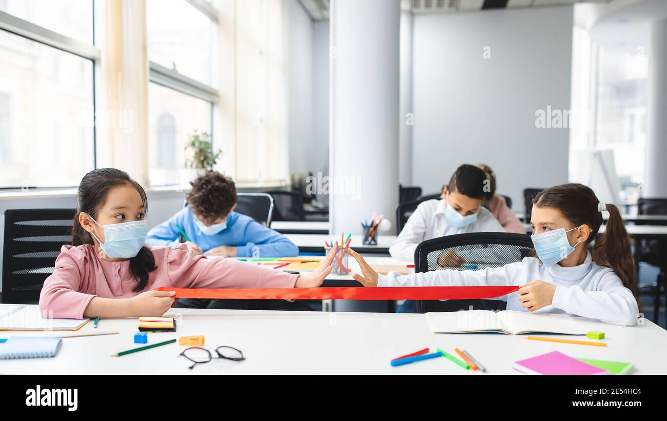 Diverse children wearing face masks keeping distance at arm's length ...