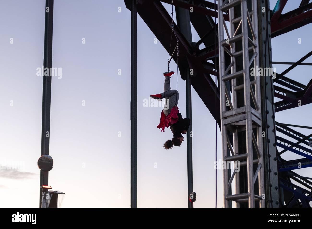Female acrobat artist stunt hanging suspended from cable on Tyne bridge ...