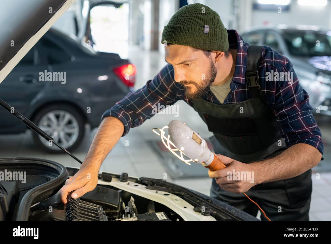 Young serious professional repairman in workwear holding lamp and ...