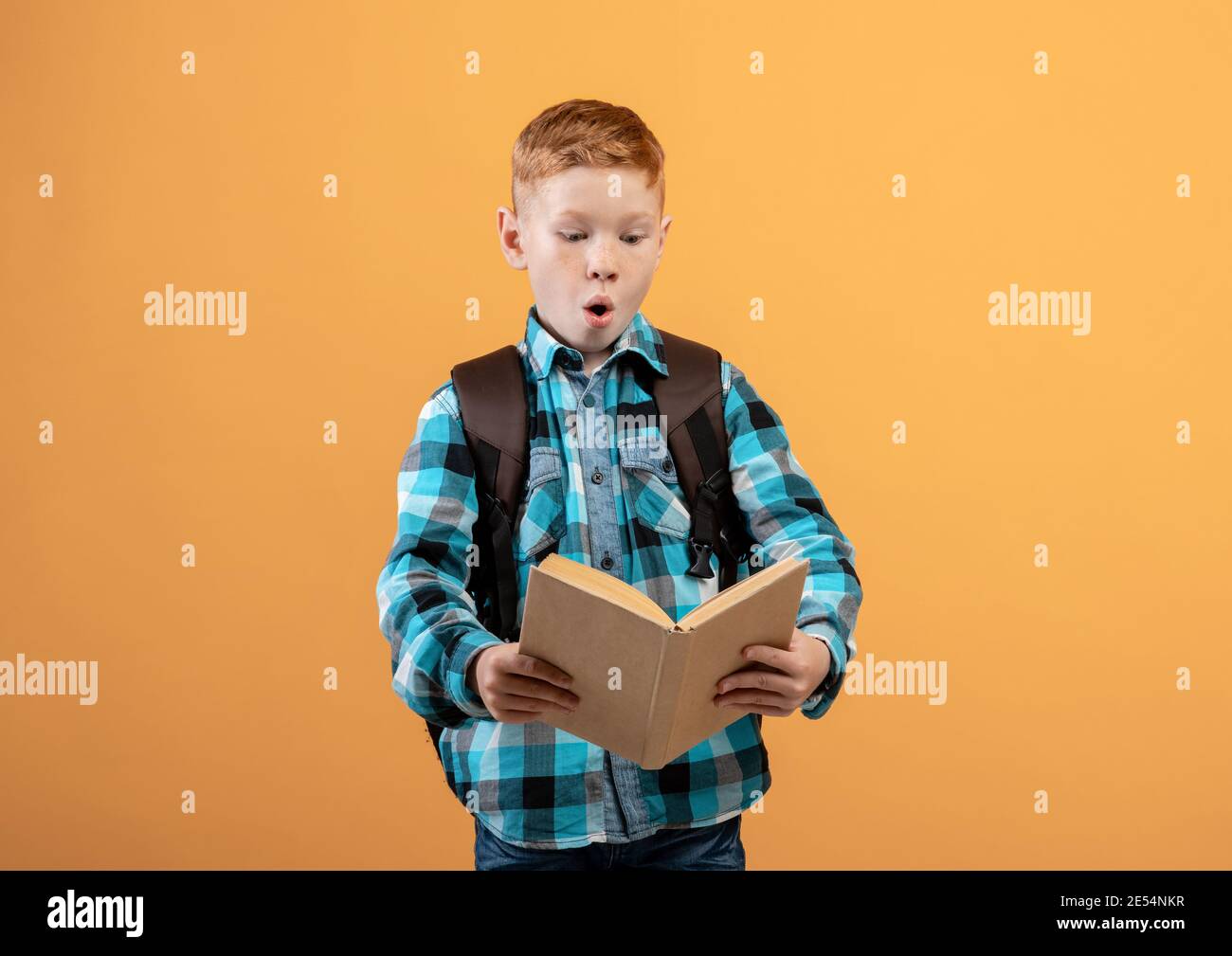 Amazed ginger boy schooler reading book on yellow background Stock ...