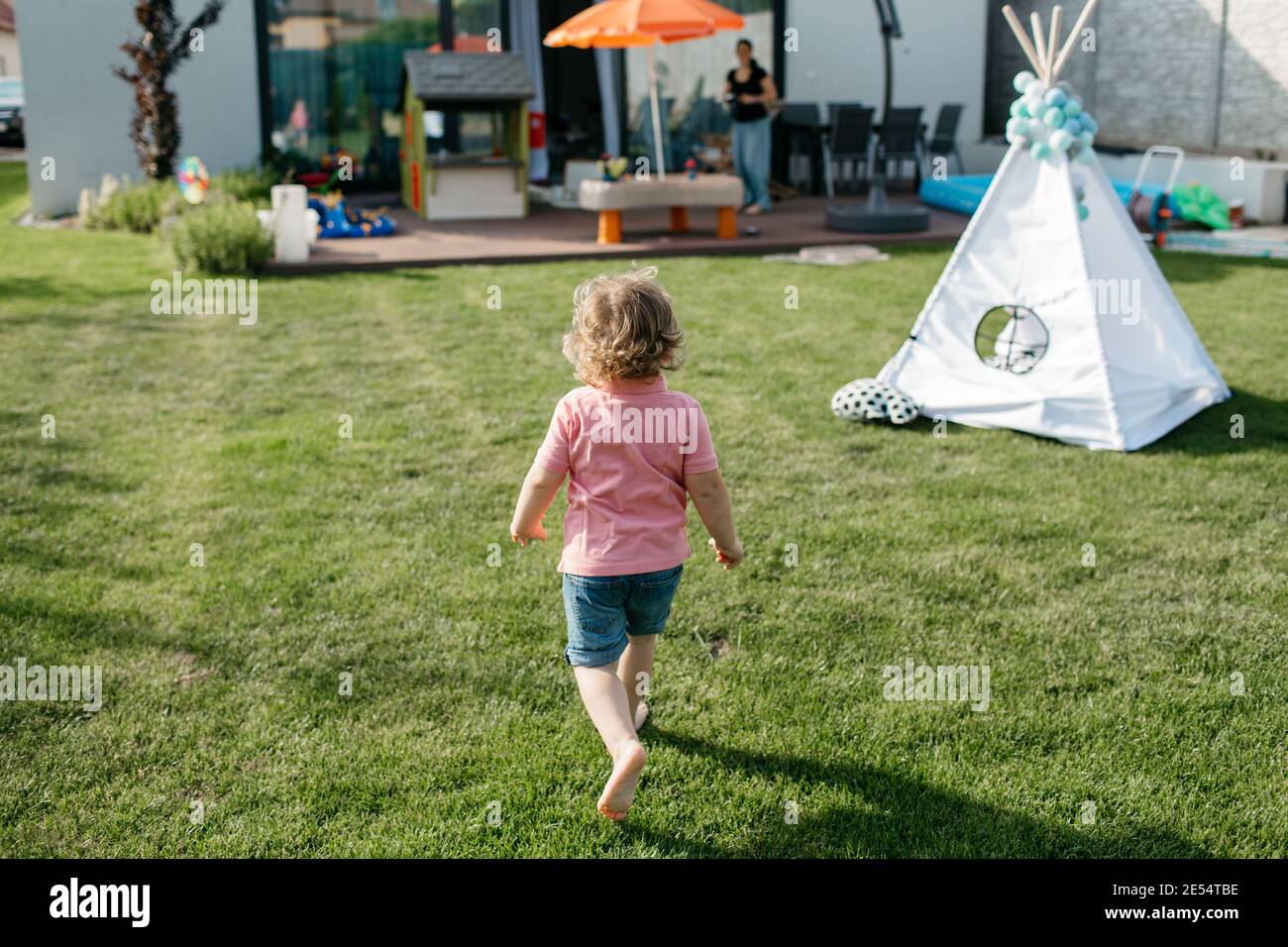 Rear view of a child walking towards his mother across a garden. Back ...