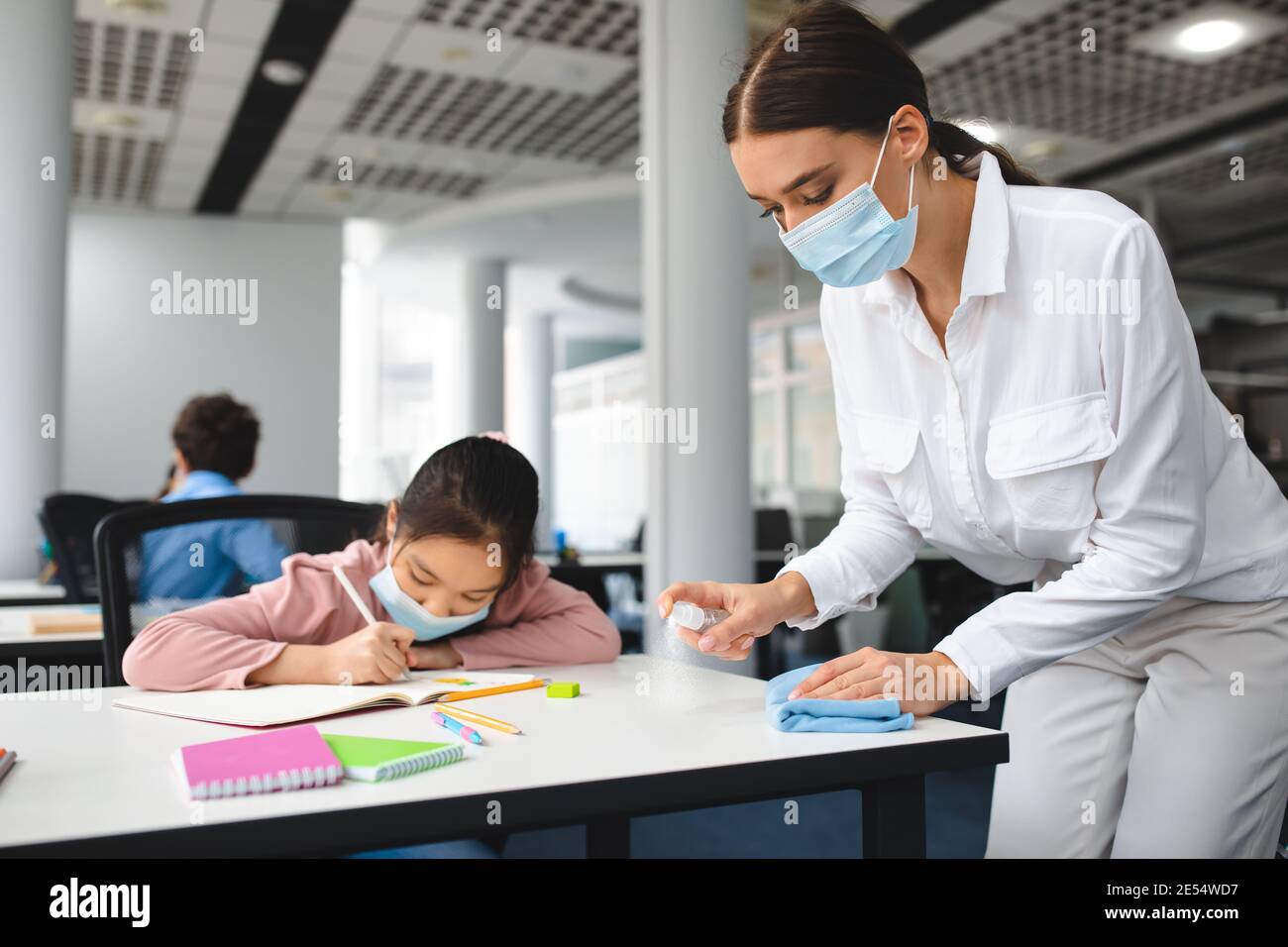 Teacher in mask cleaning table with antibacterial sanitizer and napkin ...