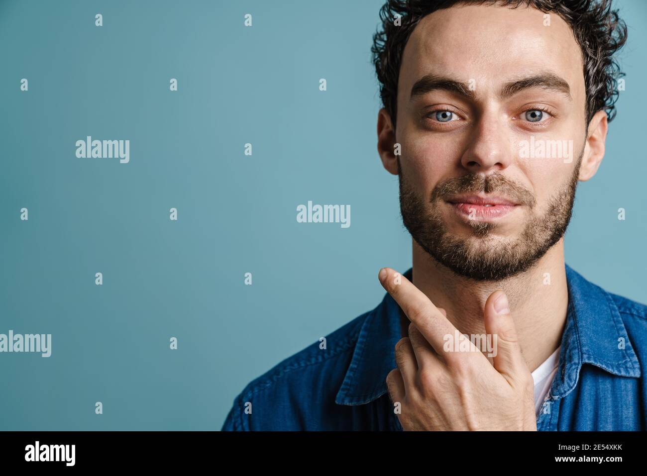 Pleased handsome guy posing and looking at camera isolated over blue ...