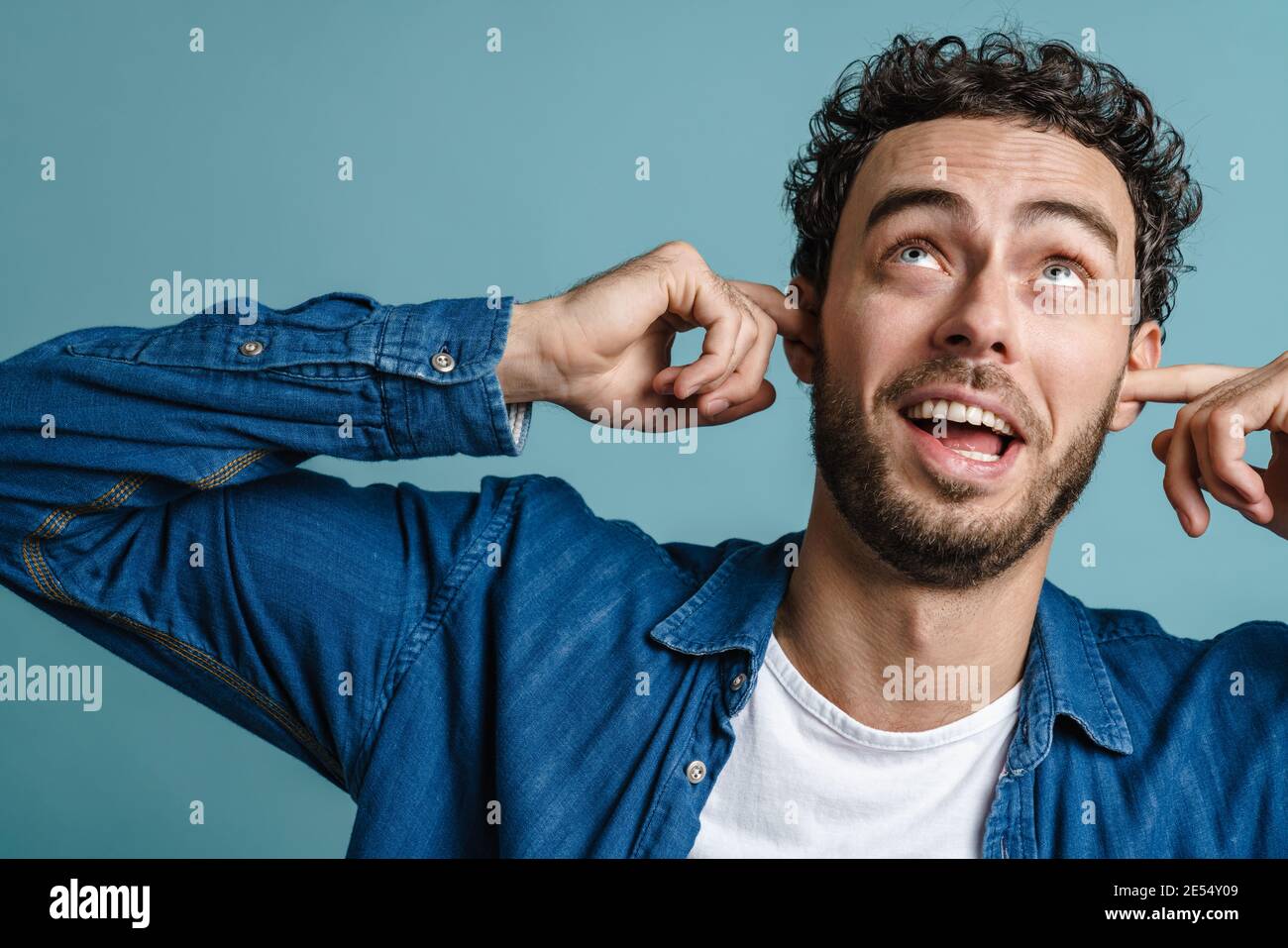 Cheerful handsome guy smiling and plugging his ears isolated over blue ...