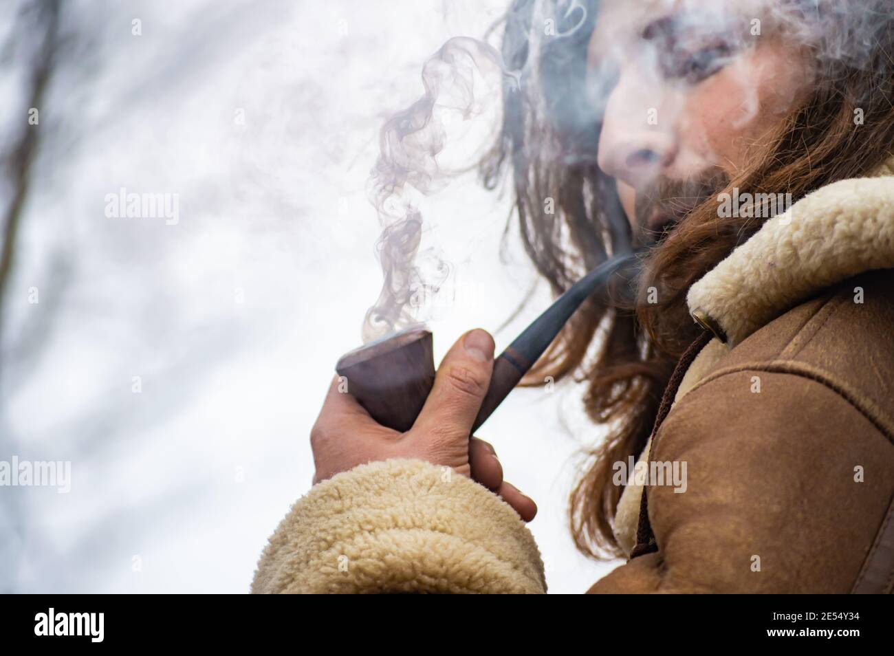 Portrait shot of a young man with a sheepskin winter coat smoking a ...