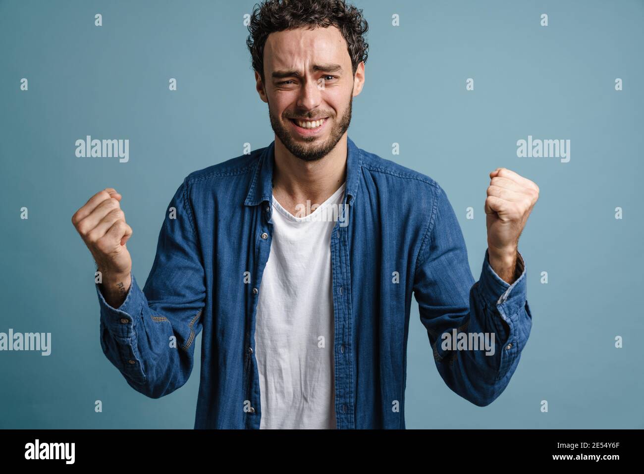 Unhappy handsome guy posing with fists up on camera isolated over blue ...