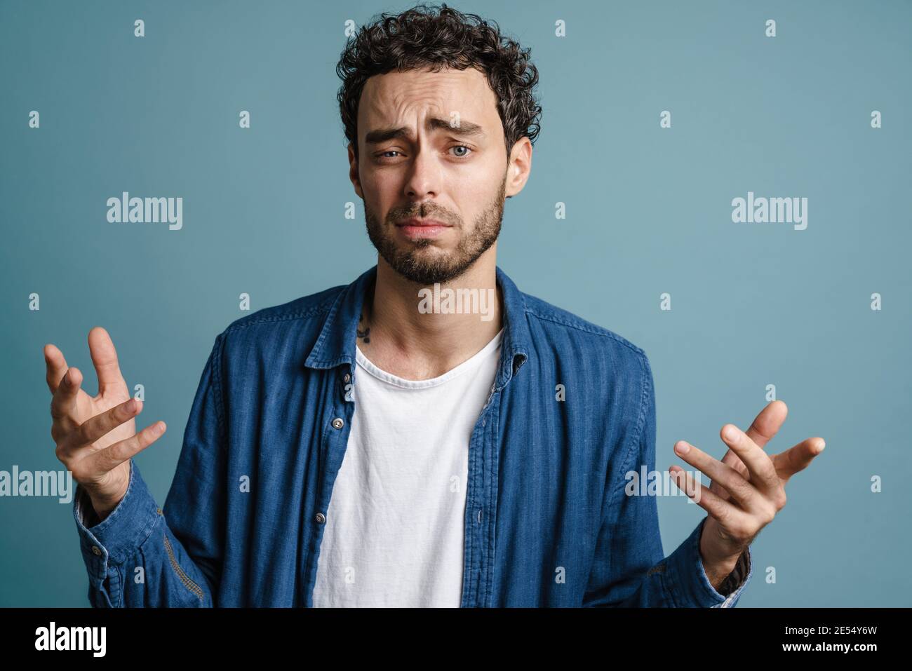 Confused handsome guy posing with hands-up at camera isolated over blue ...