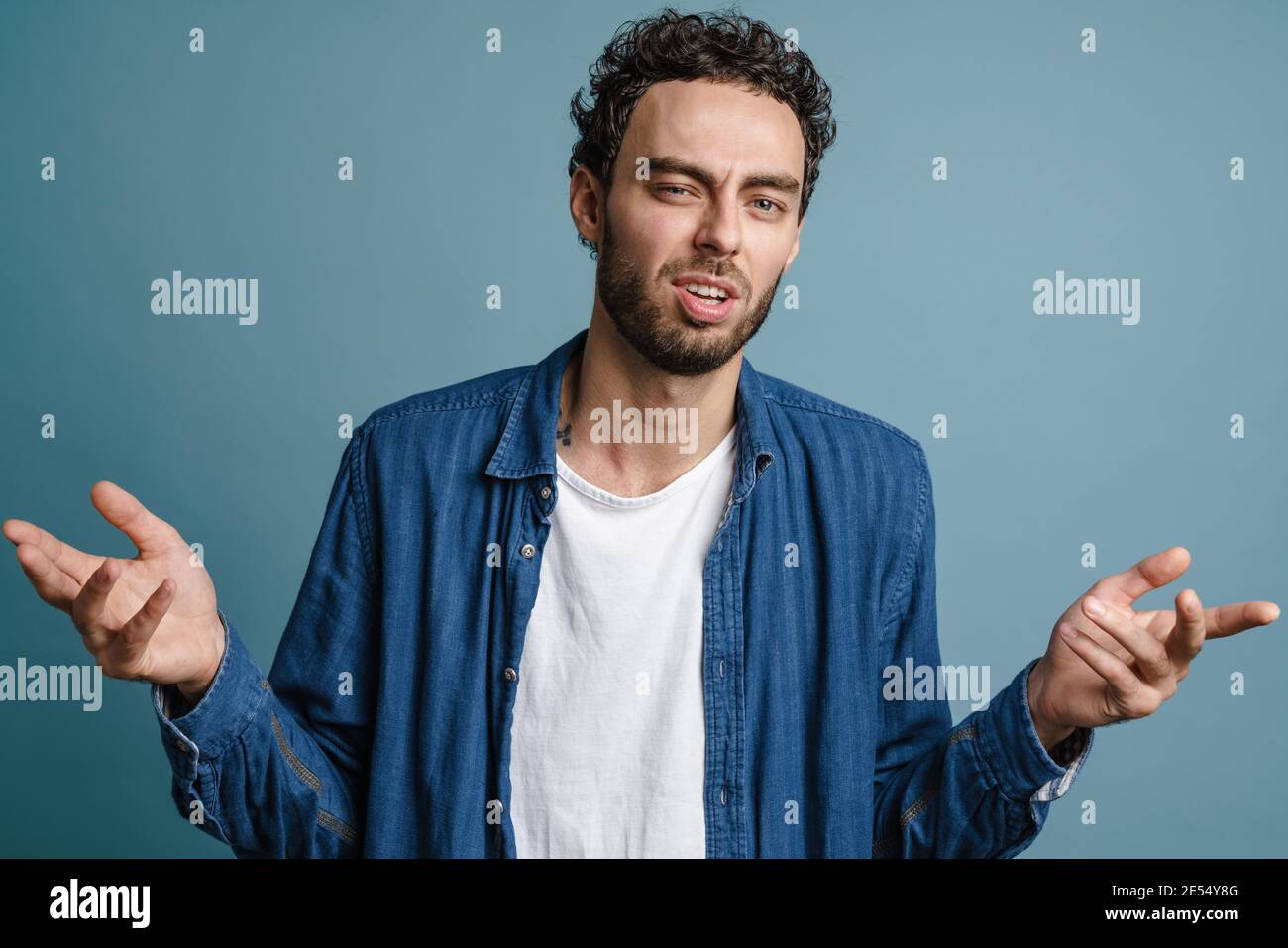 Confused handsome guy posing with hands-up at camera isolated over blue ...
