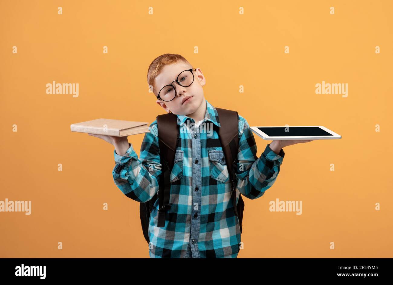 Confused kid schooler holding digital tablet and book Stock Photo - Alamy