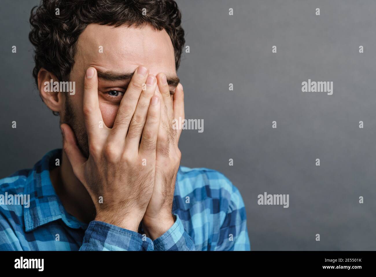 Caucasian scared guy posing and covering his face isolated over grey ...