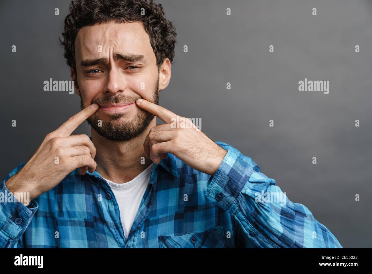 Unhappy handsome guy making smile on his face with fingers isolated ...