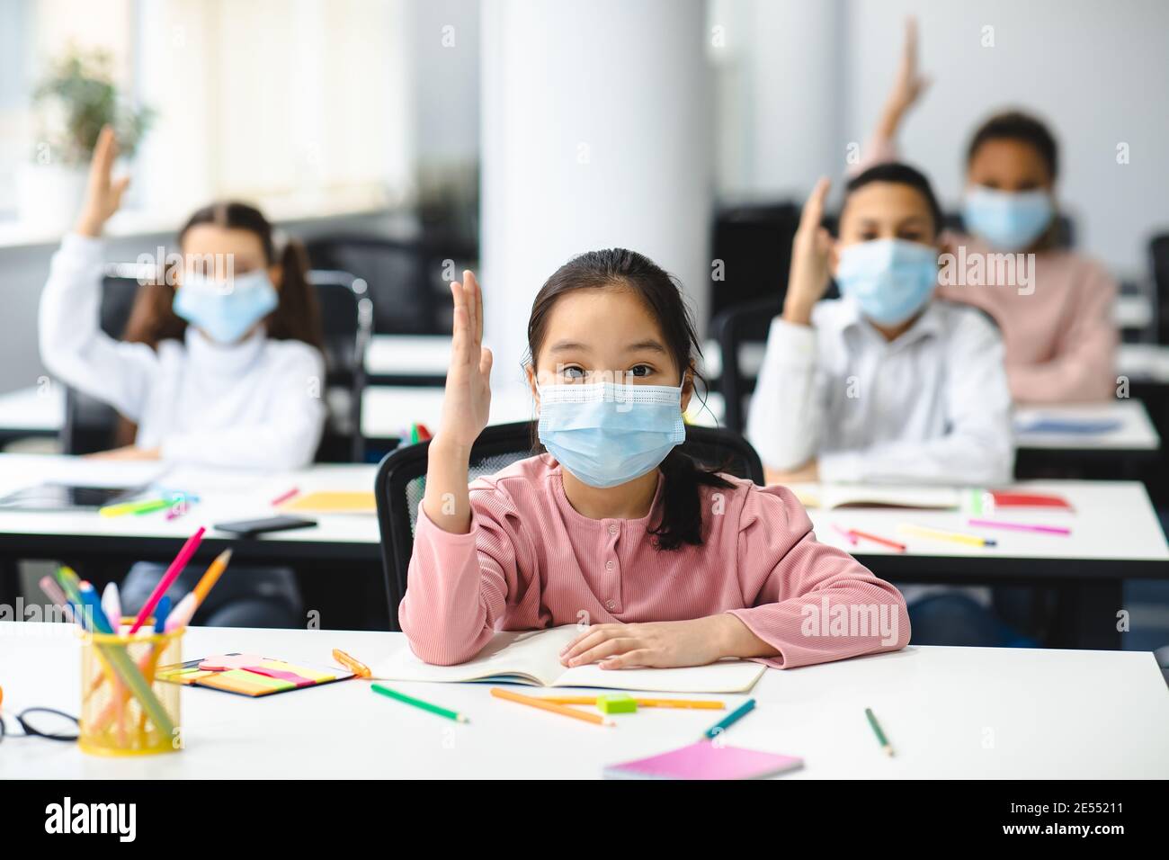 Schoolchildren raising hands at classroom, wearing medical masks Stock ...