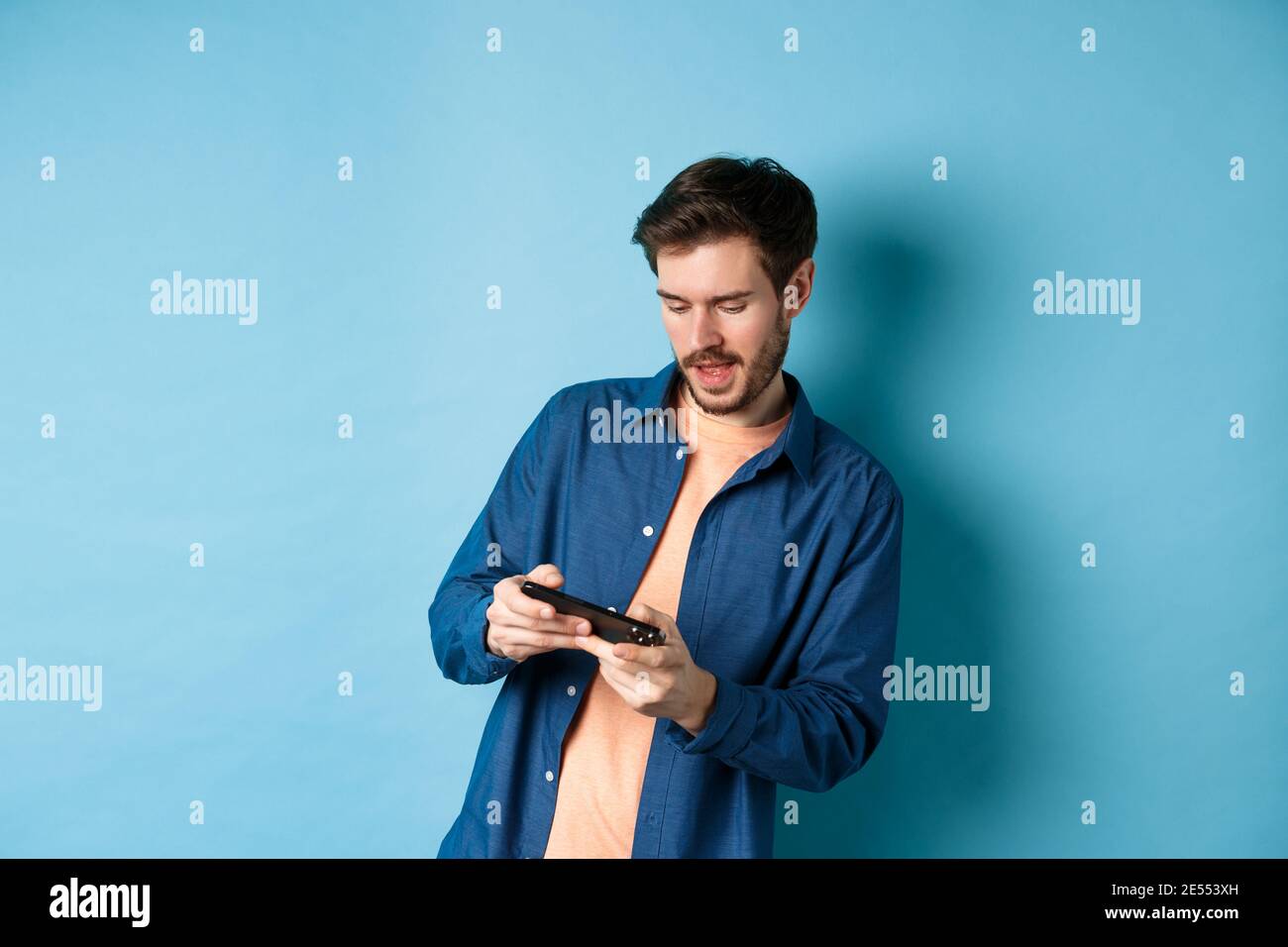 Young guy playing video game on mobile phone, tilt body and holding ...