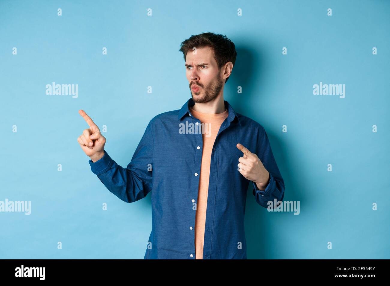 Confused and annoyed guy pointing and looking left at empty space with ...