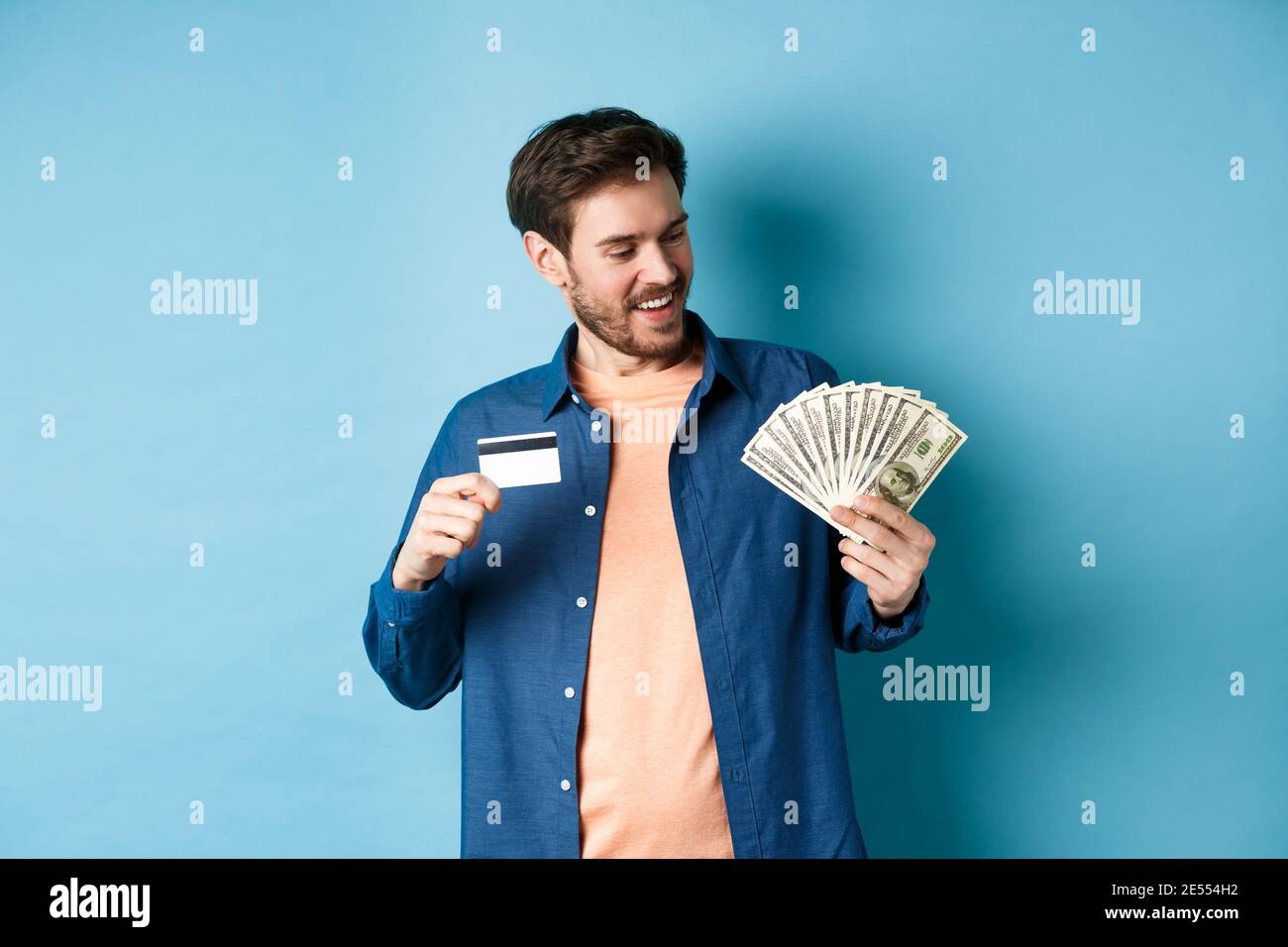 Smiling modern guy looking at cash and showing plastic credit card ...