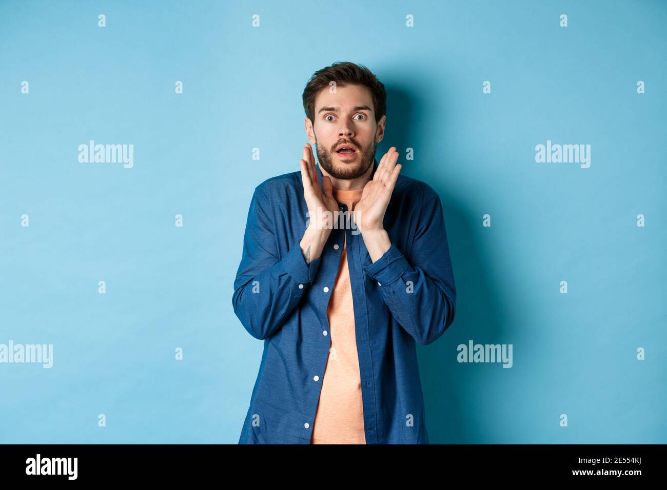 Shocked and scared young man standing in stupor, raising hands up and ...
