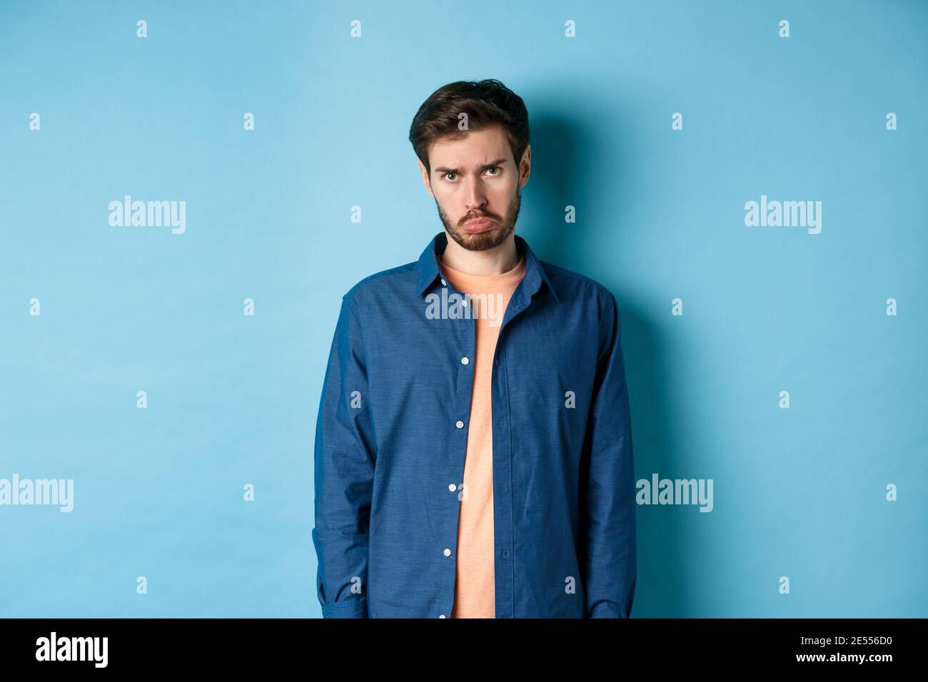 Sad and gloomy young man sulking, pulling miserable face and looking ...