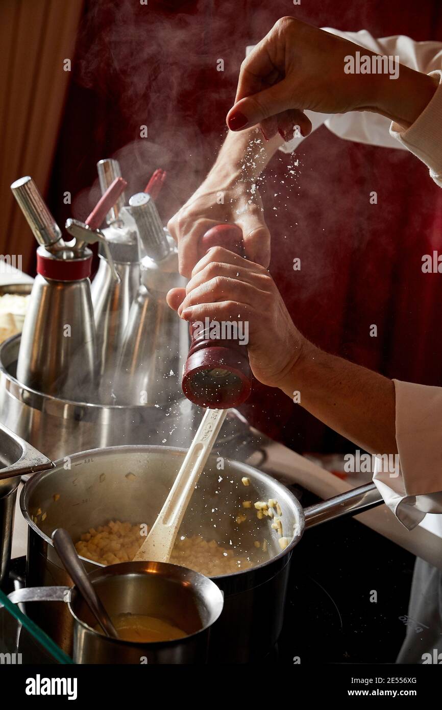 Woman's hands as she puts a pinch of salt and turns a pepper grinder or ...