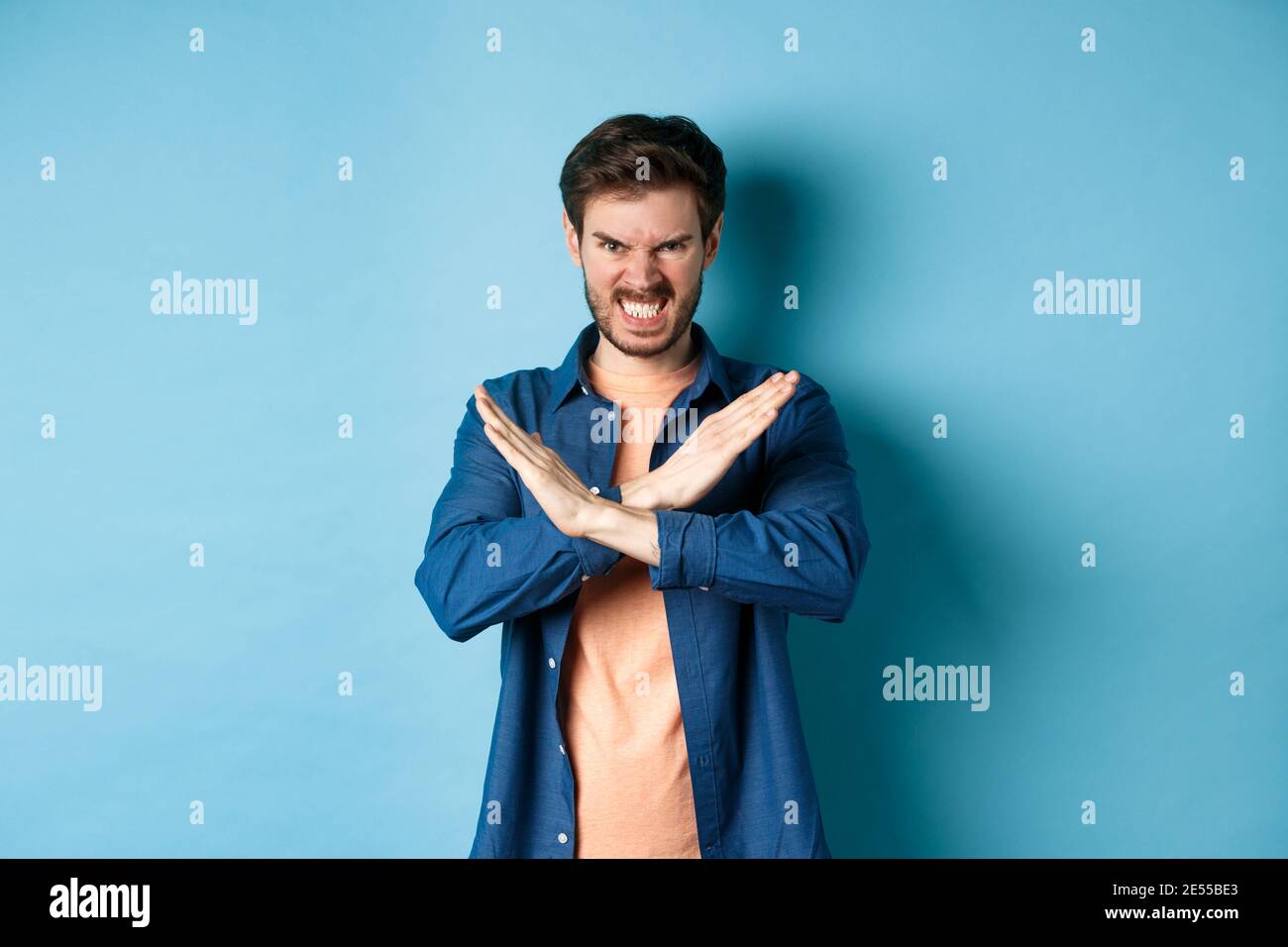 Angry young man frowning and clenching teeth outraged, showing cross ...