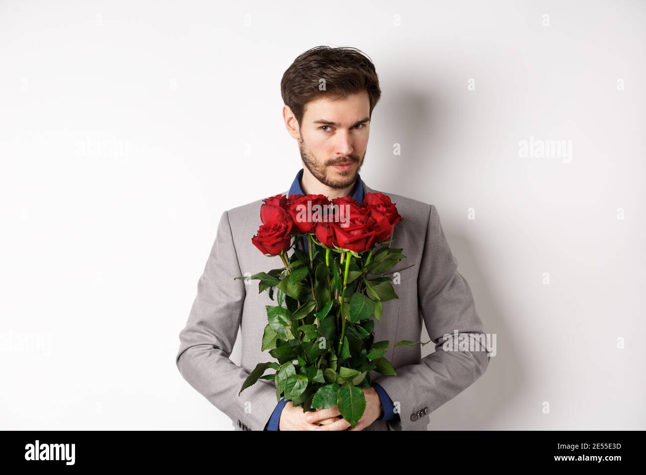 Handsome macho man going on date in suit, holding bouquet of red roses ...