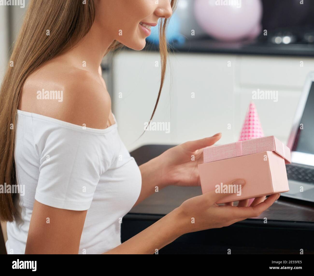 Close up of cheerful woman opening gift box while staying at home alone during her birthday ...