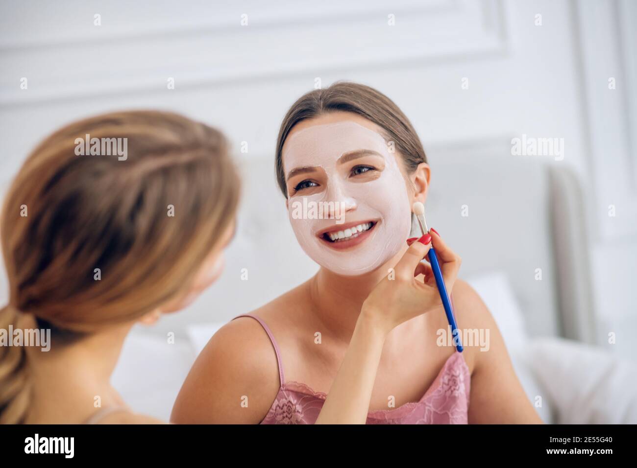 Blonde girl applying facial mask on her smiling friends face Stock ...