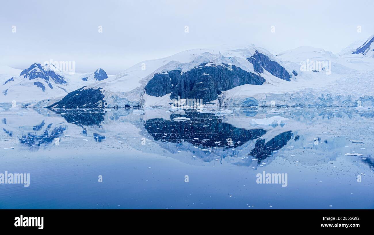 reflections of mountains and the snowy and blue ice of a glacier in the ...
