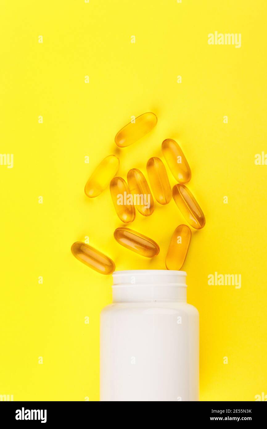 Vitamin D yellow pills on yellow background and white plastic jar ...