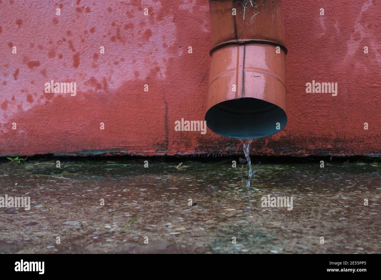 A thin trickle of water flowing from the red metal drain pipe on the ...