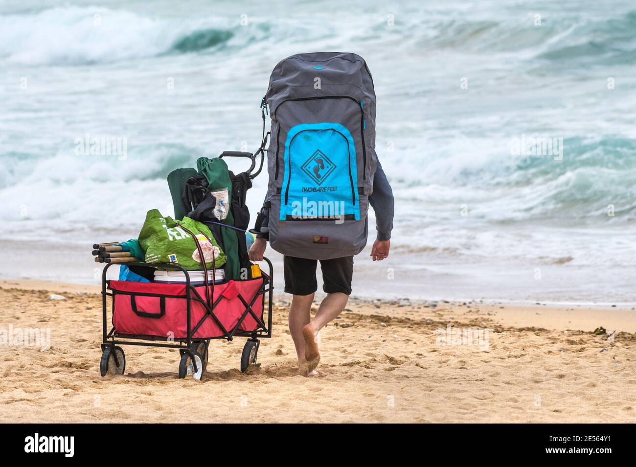 A holidaymaker dragging a trolley full of beach equipment on Fistral ...