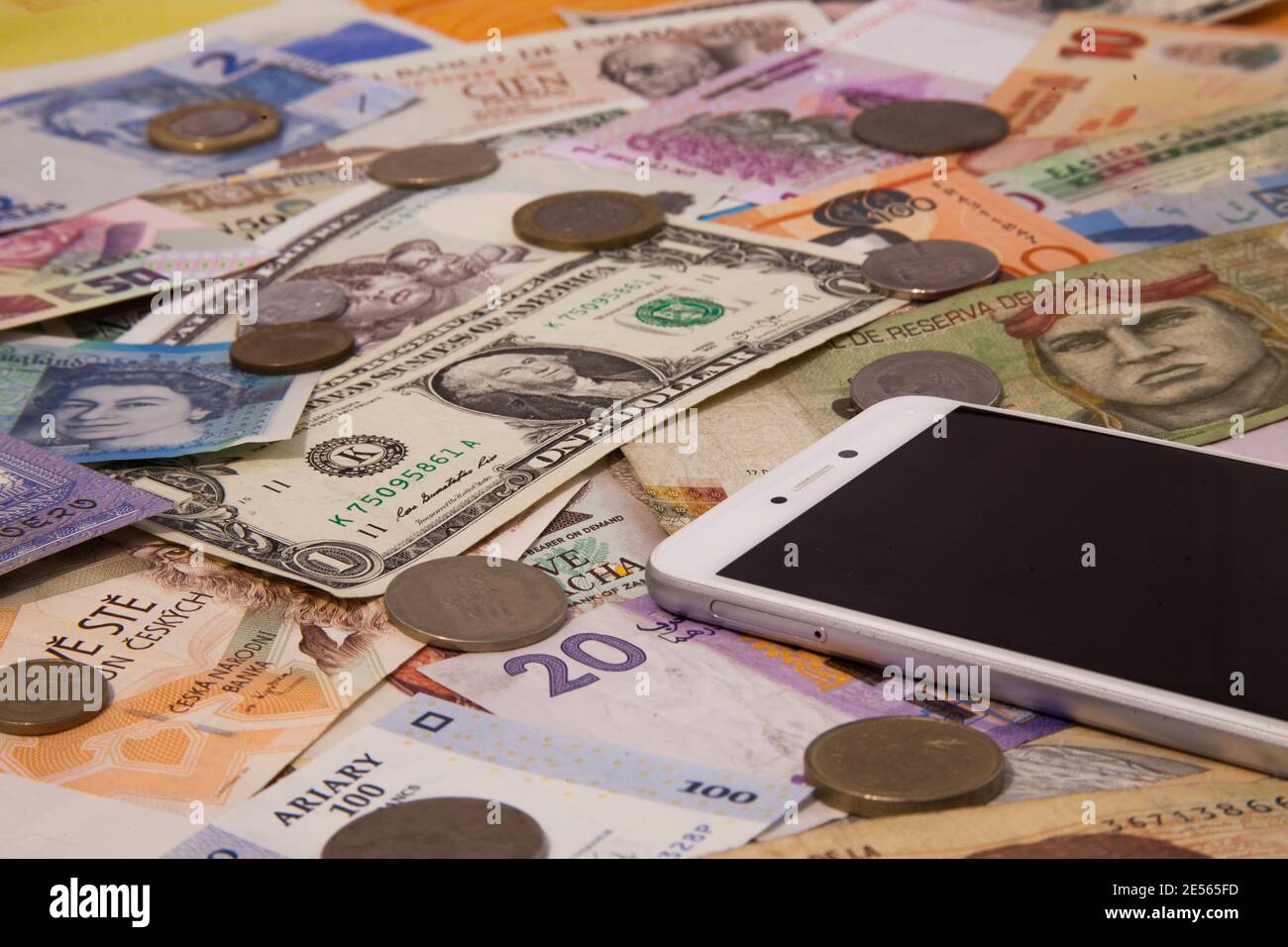 Closeup of a smartphone on different cash bills and coins on the table ...