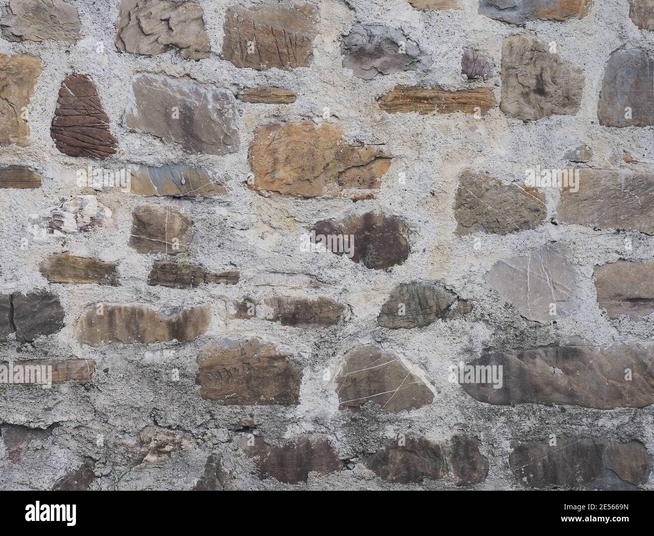 A wall with masonry of various shapes of stone and a thick gray layer ...
