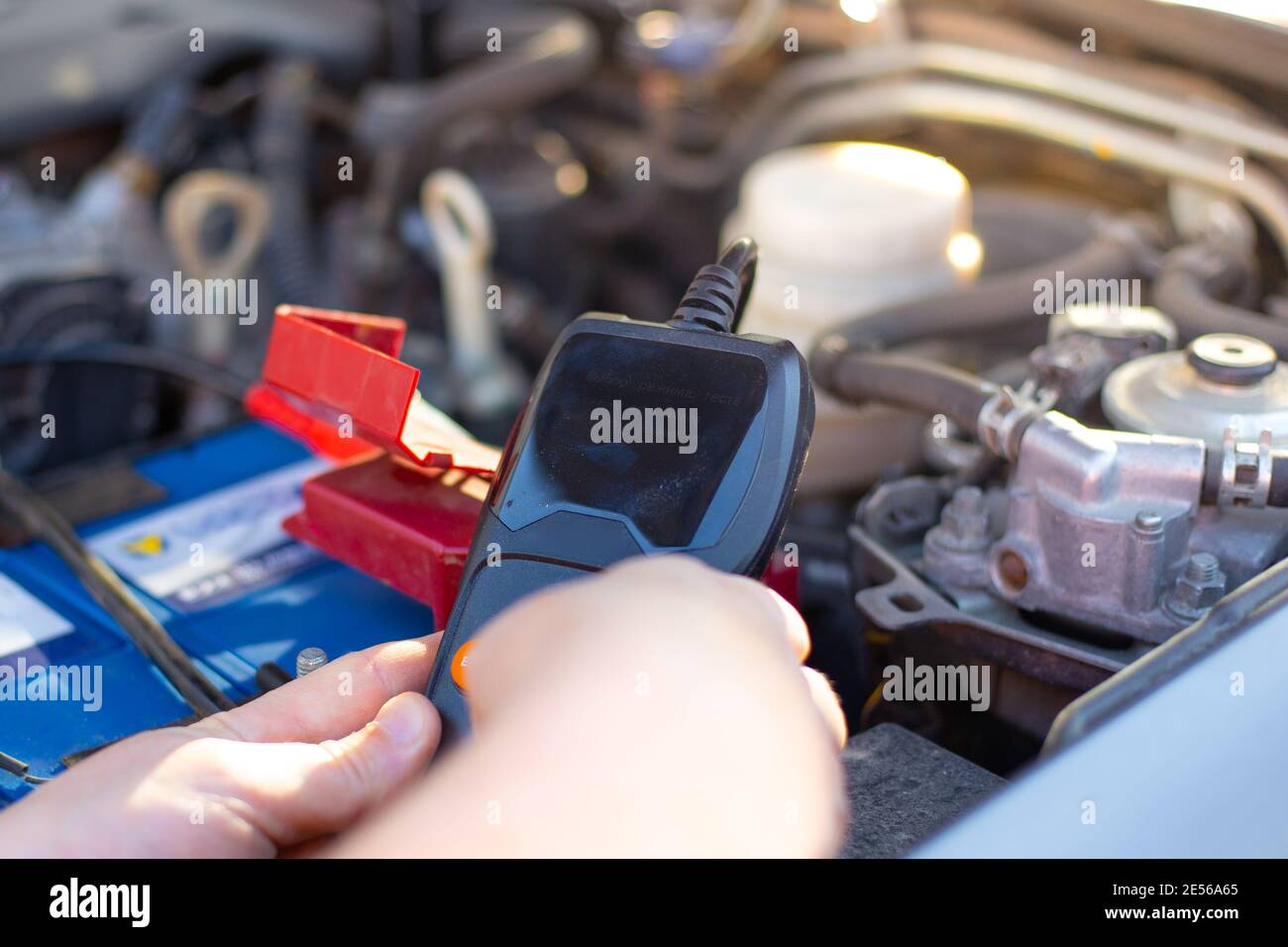 a car mechanic under the hood of a car diagnoses a car battery with a ...