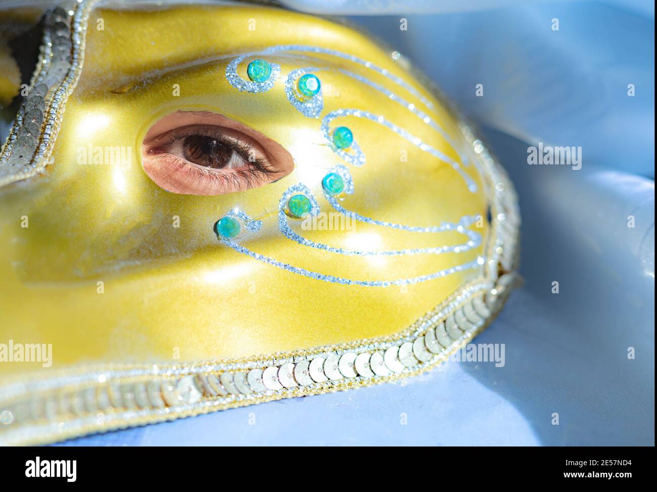 Selective focus of an eye and a carnival mask with a bluish fabric ...