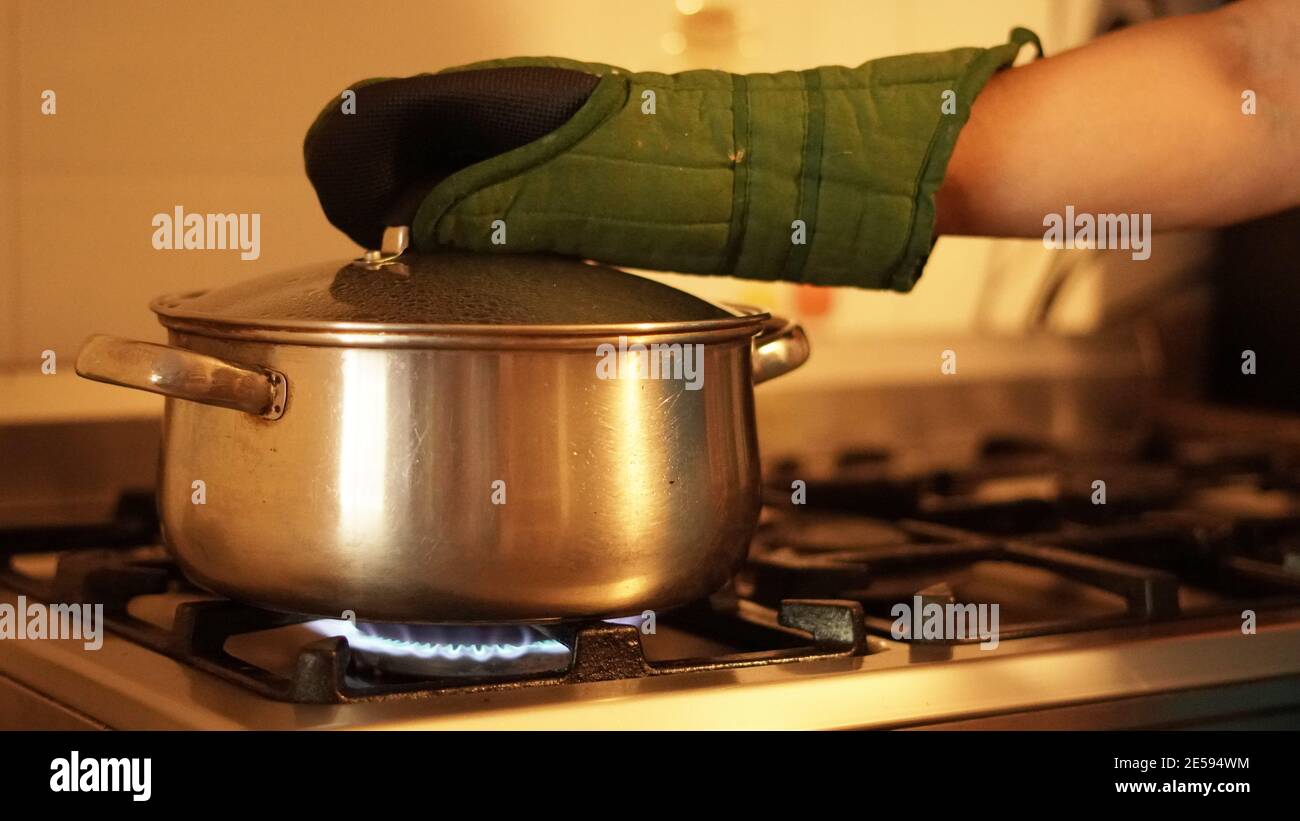 Closeup shot of a pan on a stove and a human hand with a kitchen glove ...