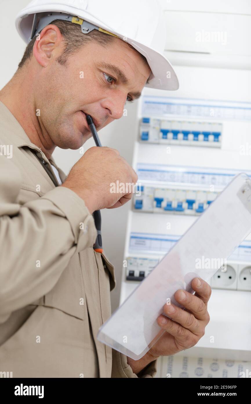 electrician stood by fusebox reading clipboard and chewing pen Stock ...