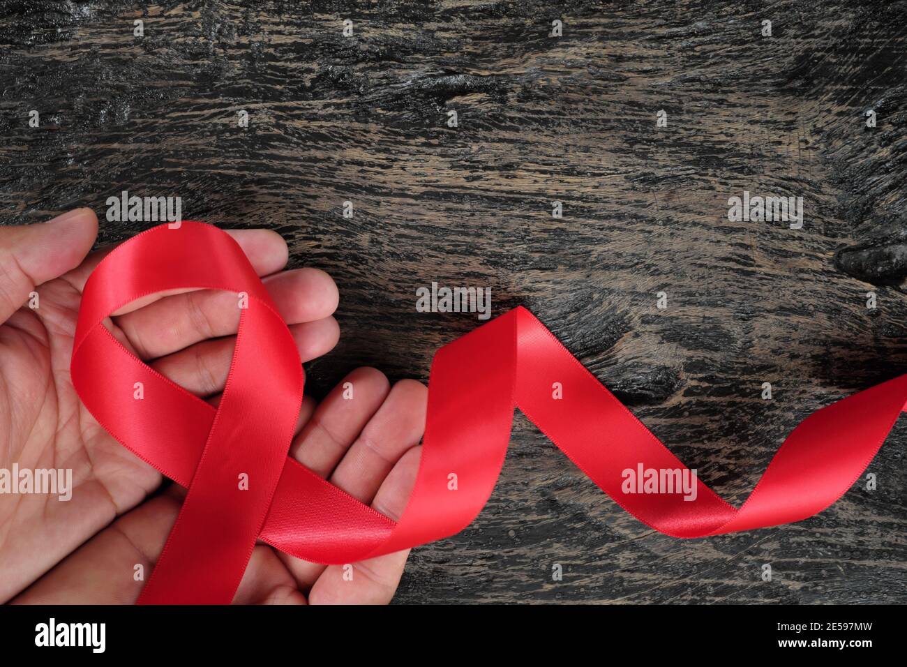 Top view of male hand holding red ribbon on dark wood background. AIDS ...