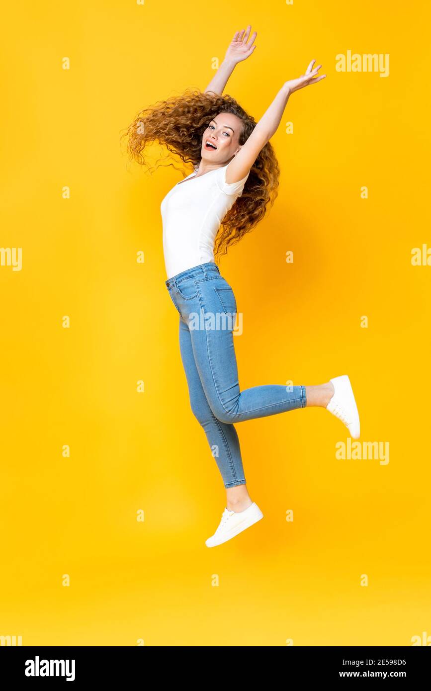 Pretty woman jumping freely with both hands up isolated in yellow color ...