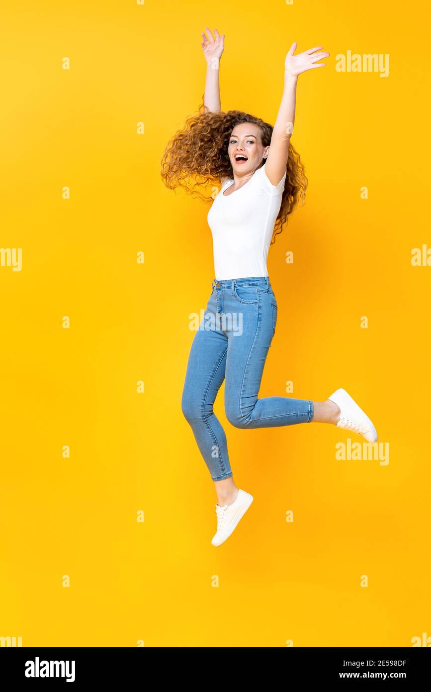 Pretty woman jumping freely with both hands up isolated in yellow color ...
