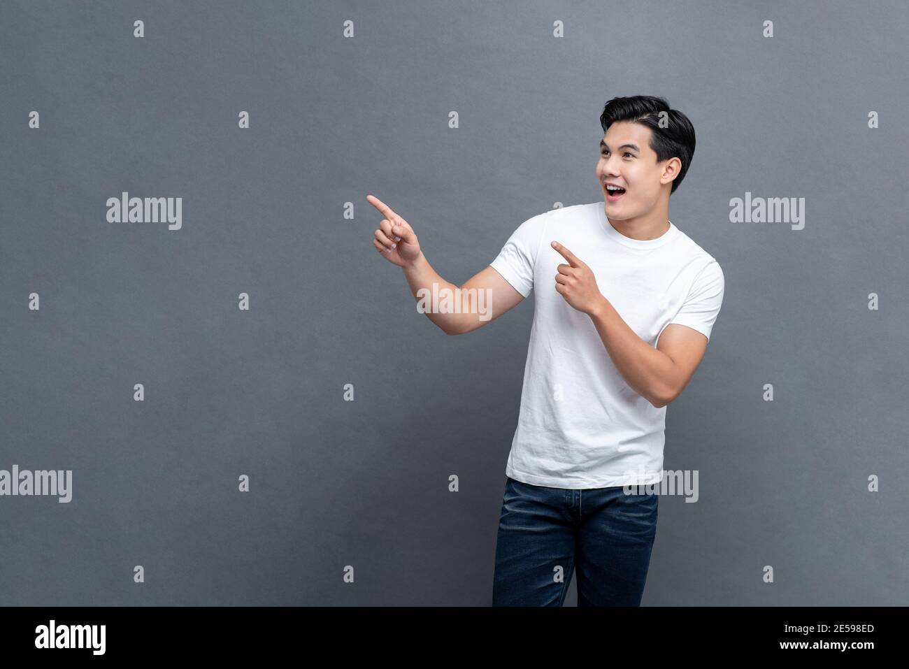 Surprised smiling young handsome Asian man in white t-shirt looking and ...