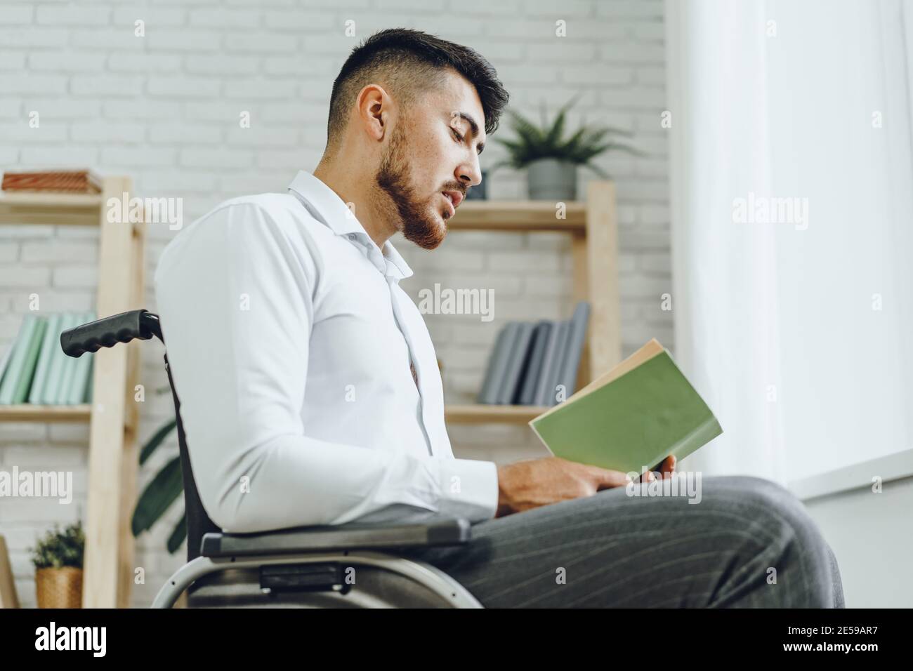 Disabled man in wheelchair reading a book indoors Stock Photo - Alamy