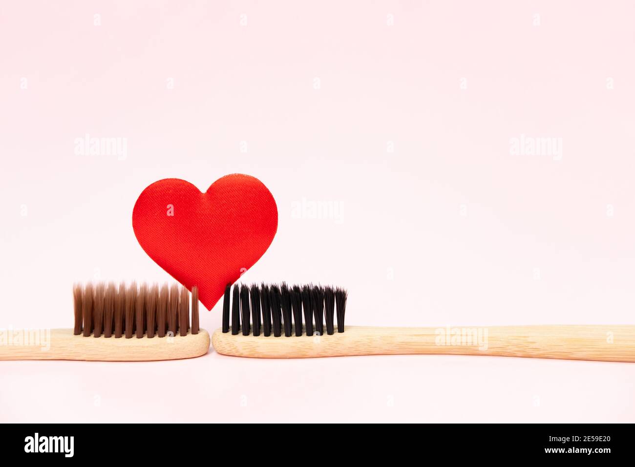 Two bamboo toothbrushes with red heart on pink background with copy ...