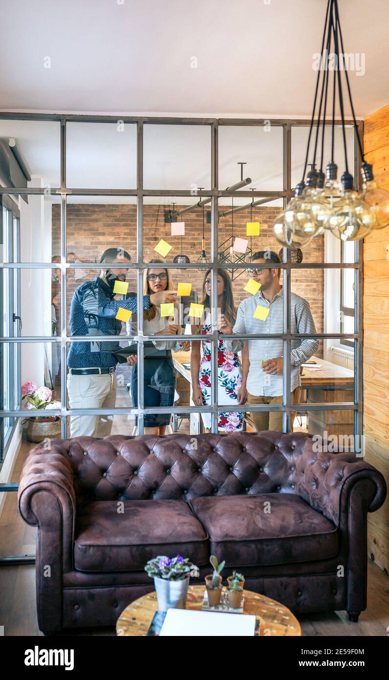 Business people in a work meeting placing sticky notes on the wall ...