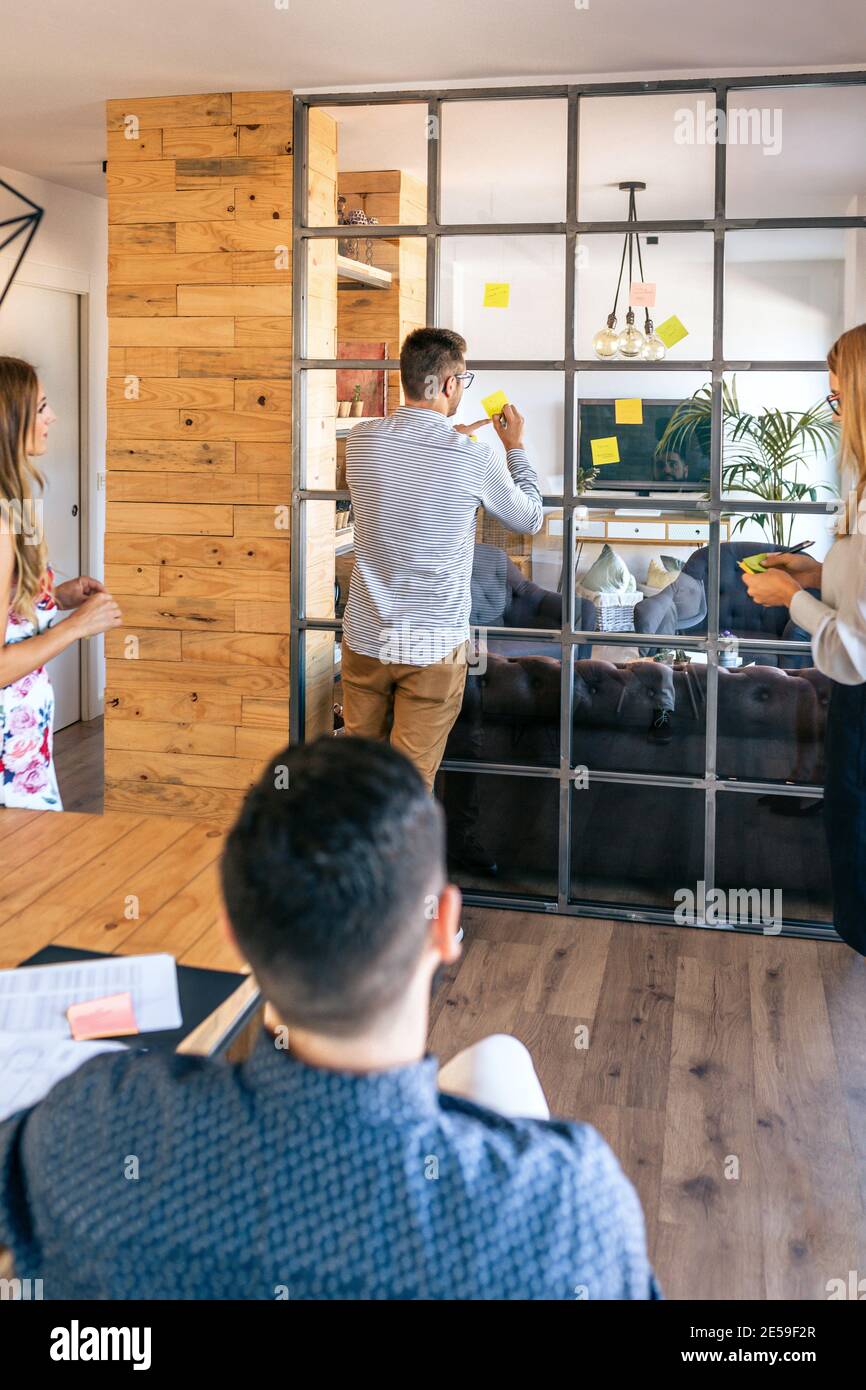 Business people in a work meeting placing sticky notes on the wall ...