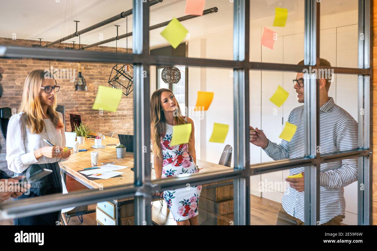 Business people in a work meeting placing sticky notes on the wall ...